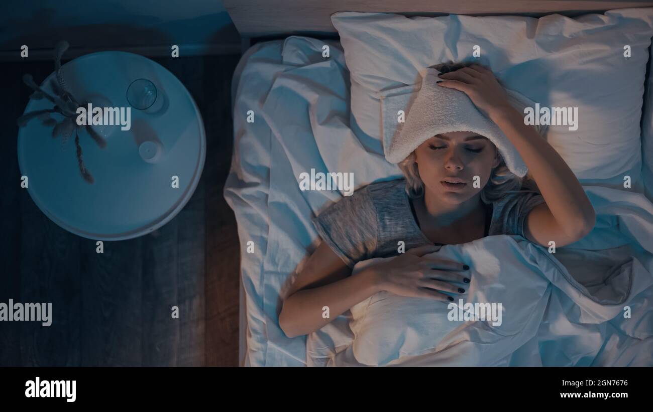 Top view of sick woman with towel on head lying on pillow in bedroom ...