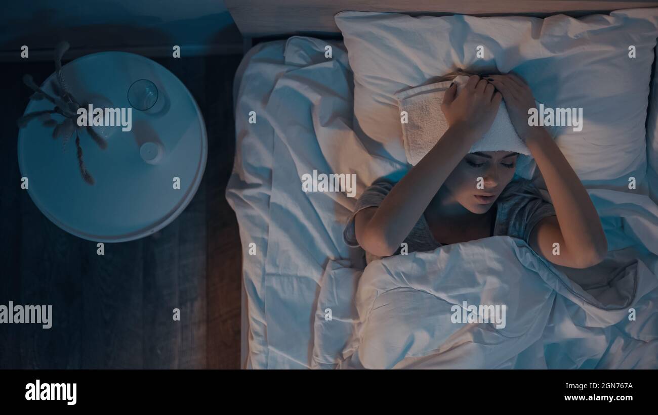 Top view of sick woman with towel on head lying on bed Stock Photo - Alamy