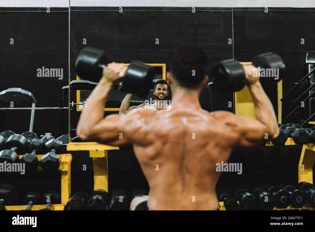 Face reflected in a mirror of a man exercising with dumbbells in a gym ...