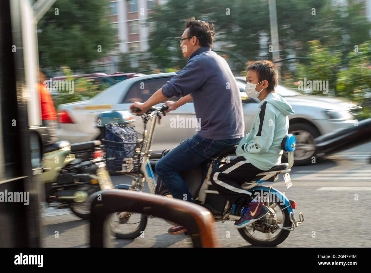 A Chinese man takes his son to school on a bicycle in the early morning ...