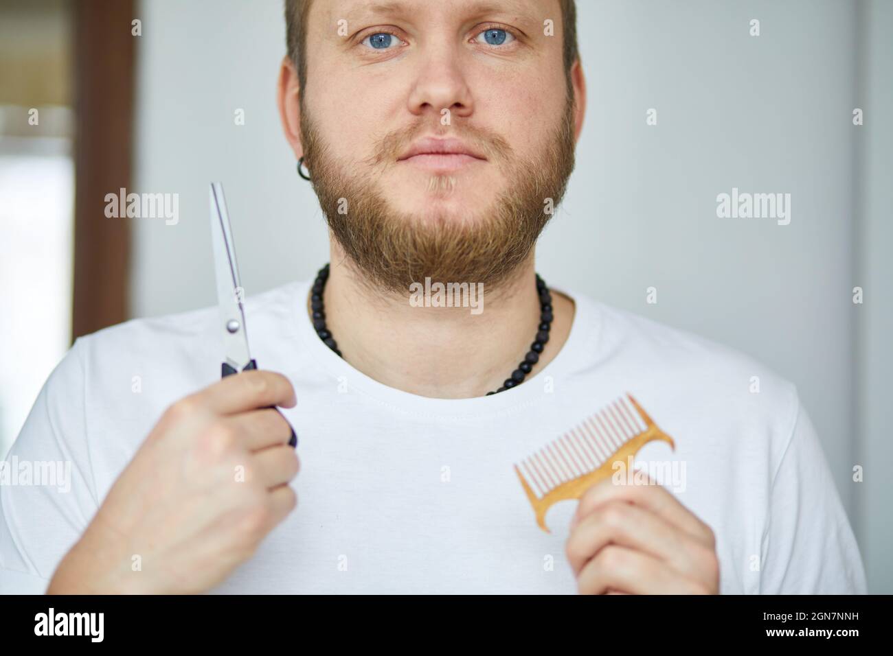 A male hairdresser wih bread holds scissors and a comb in his hands ...