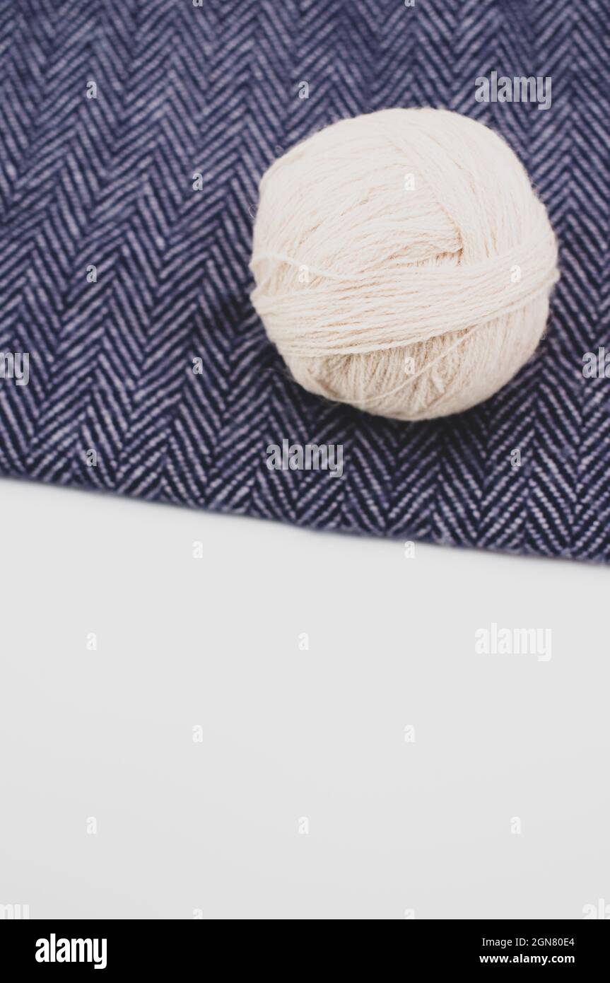 Vertical shot of soft beige yarn ball and blue cloth on a white ...