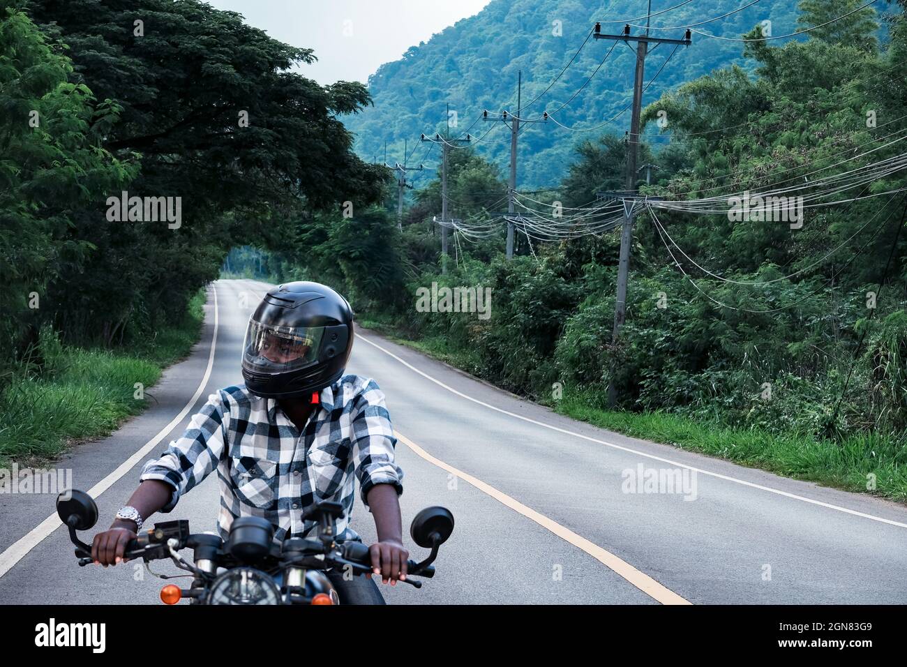 African biker man in the helmet riding a motorcycle rides on highway ...