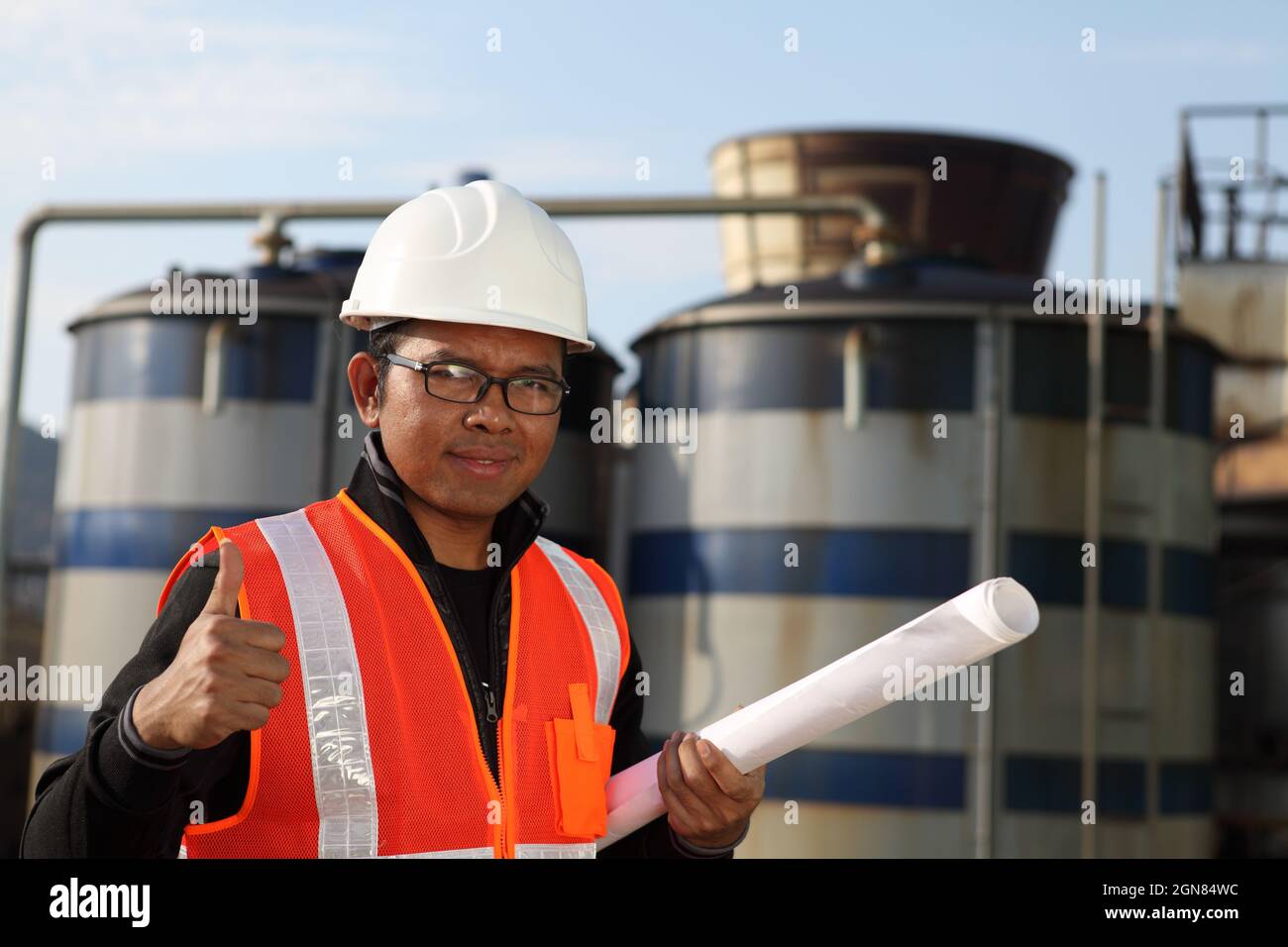 engineer standing in front of a large oil refinery with blueprint on ...