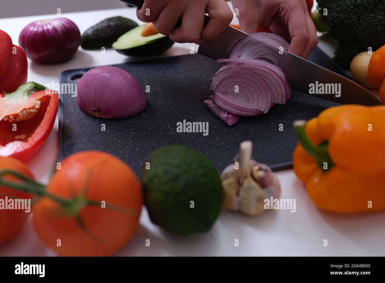 Chef cutting red onion on board among vegetables closeup Stock Photo ...