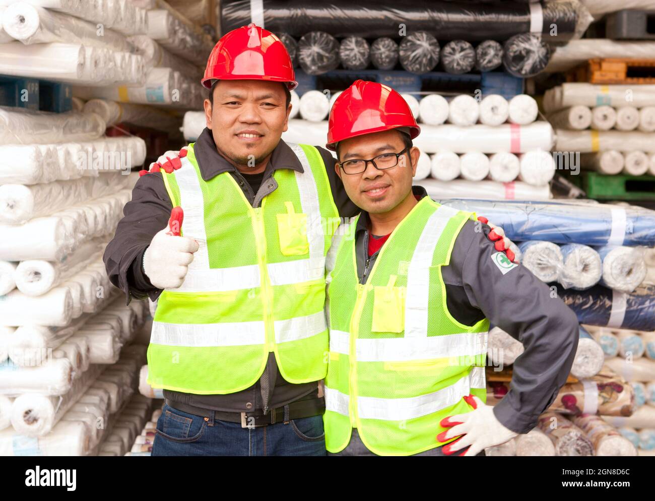 Two textile factory workers standing in werehouse raw material fabrics ...