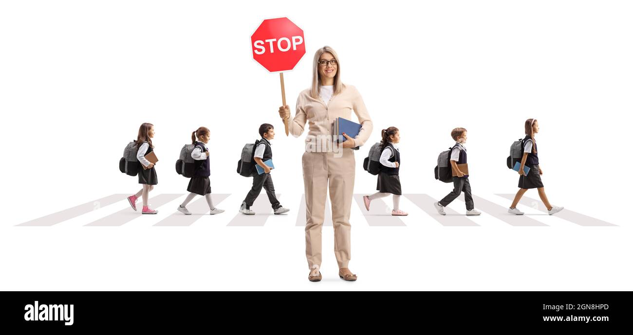Female teacher holding a stop sign and schoolchildren crossing a street ...