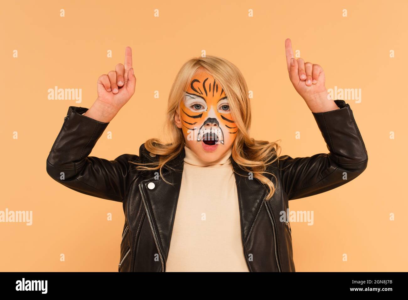 thrilled kid in tiger makeup pointing up with fingers while looking at ...