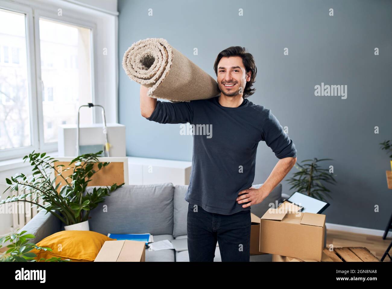 Man with hand on hip carrying rug while standing at home Stock Photo ...