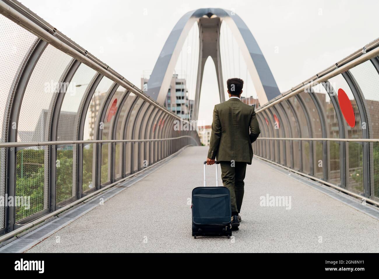 Businessman walking with wheeled luggage on bridge Stock Photo - Alamy