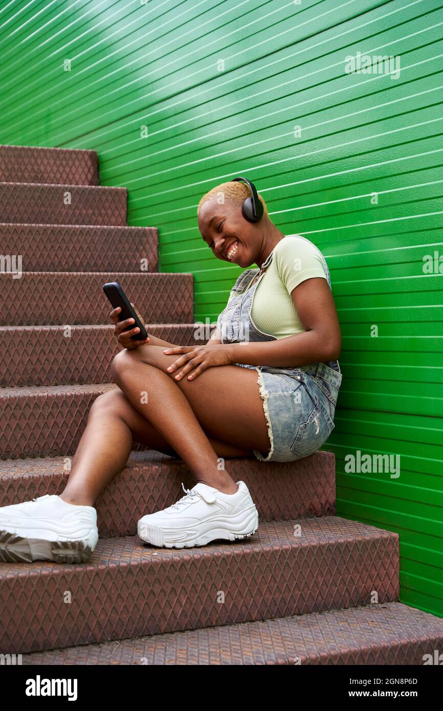 Cheerful woman text messaging through smart phone while sitting on ...