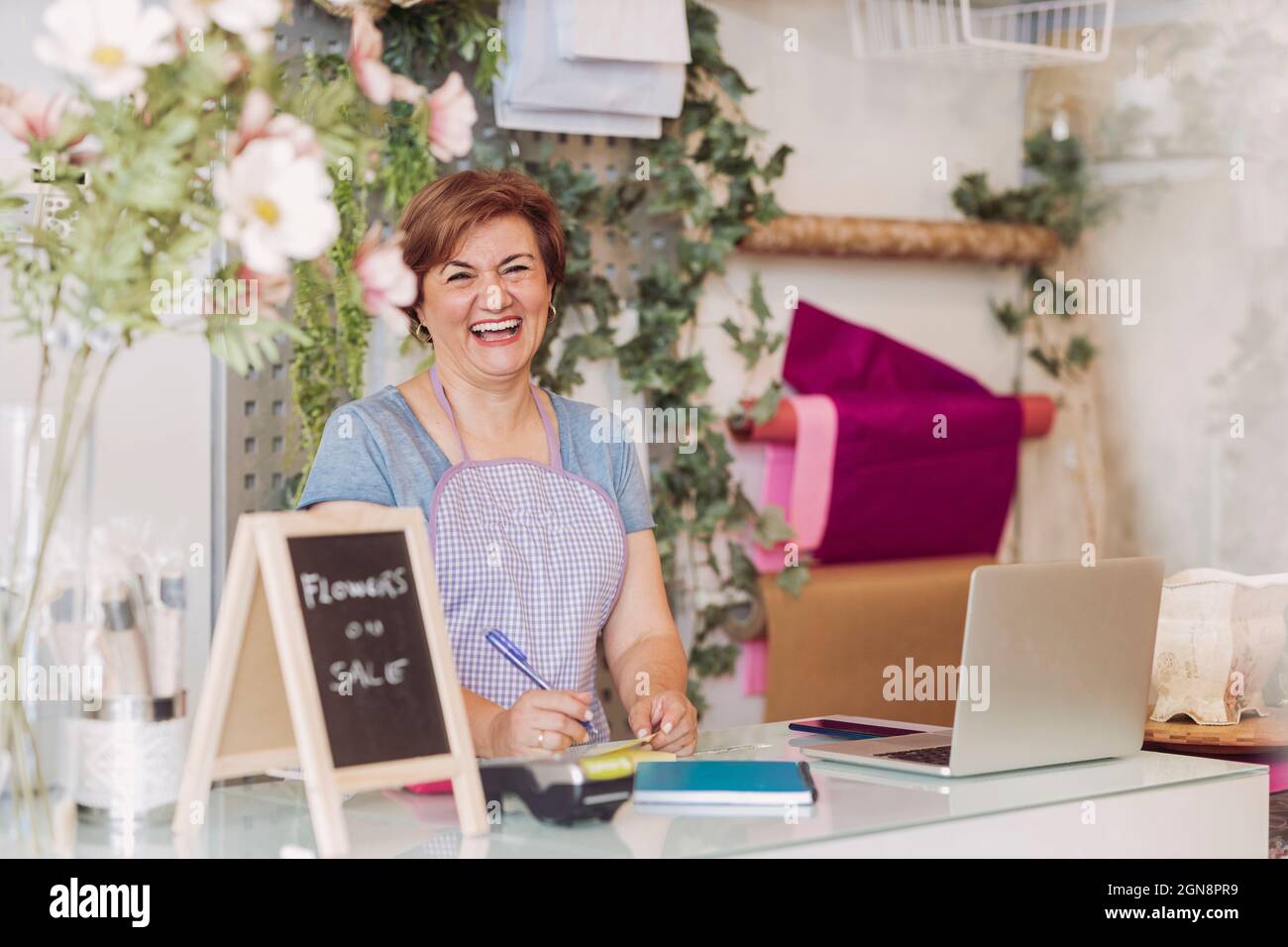 Mature female flower shop owner laughing while standing at checkout ...