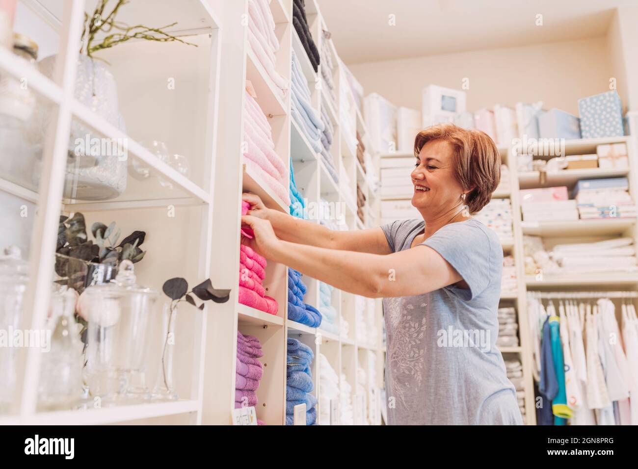 Smiling female entrepreneur arranging clothes in rack while working at ...