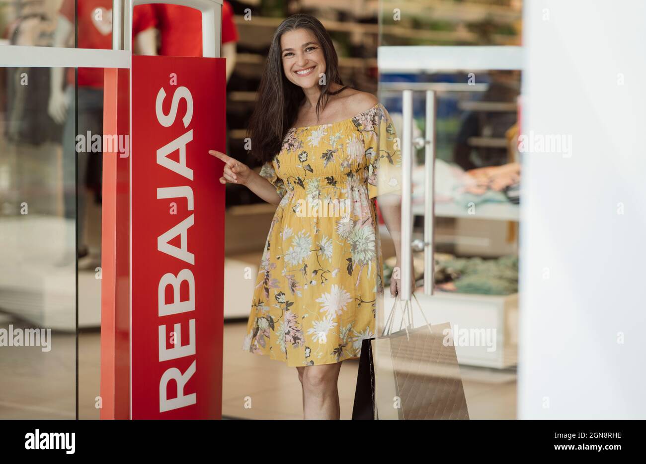 Smiling woman pointing at sign while standing in clothing store Stock ...