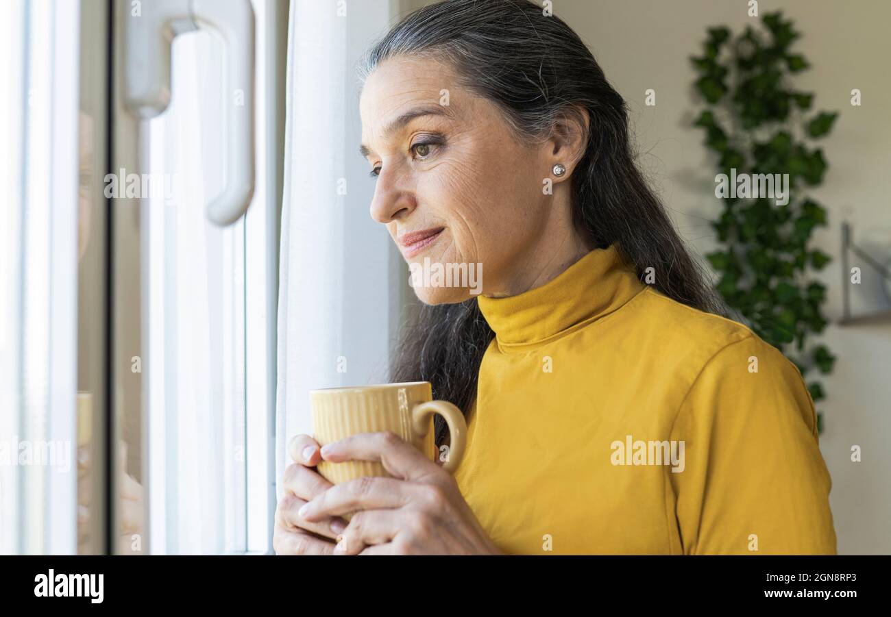 Mature woman contemplating while holding coffee mug at home Stock Photo ...