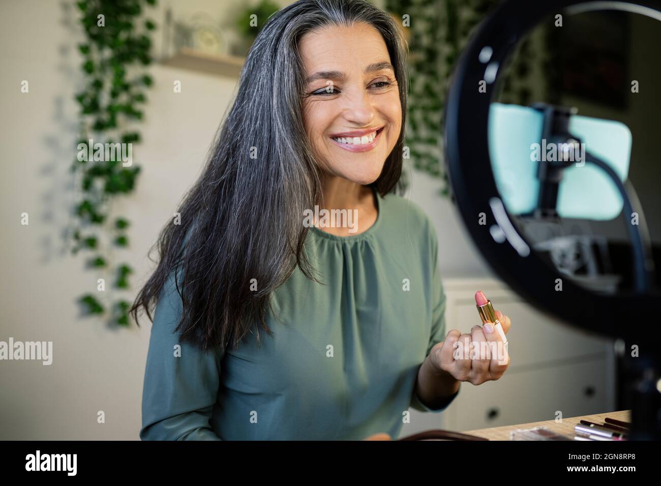 Beautiful female vlogger smiling with lipstick while vlogging at home ...