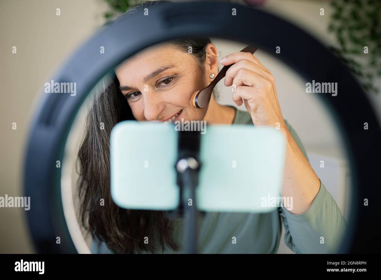 Female vlogger showing make-up tutorial seen through ring light at home ...