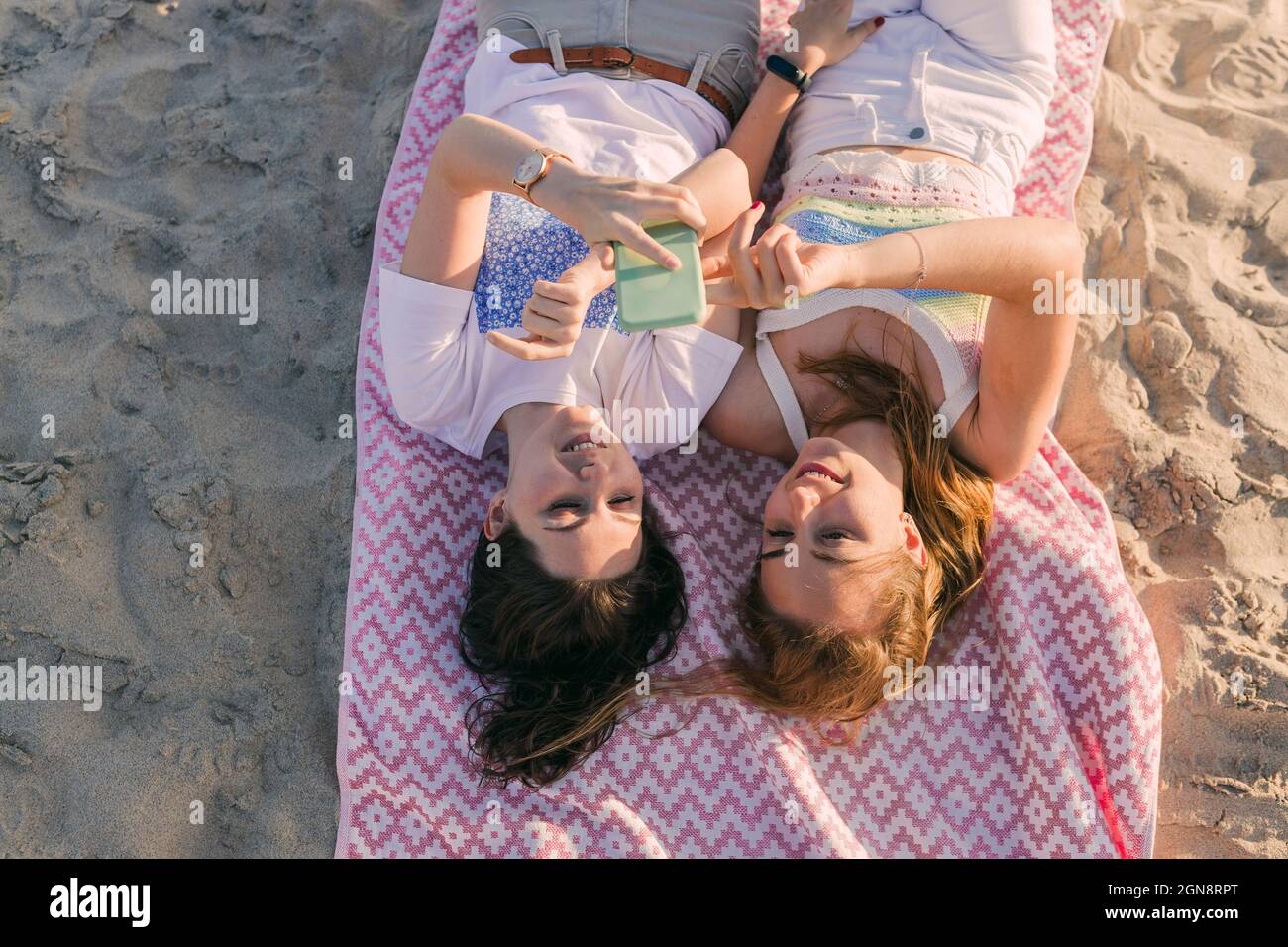 Women using mobile phone while lying on picnic blanket at beach Stock ...
