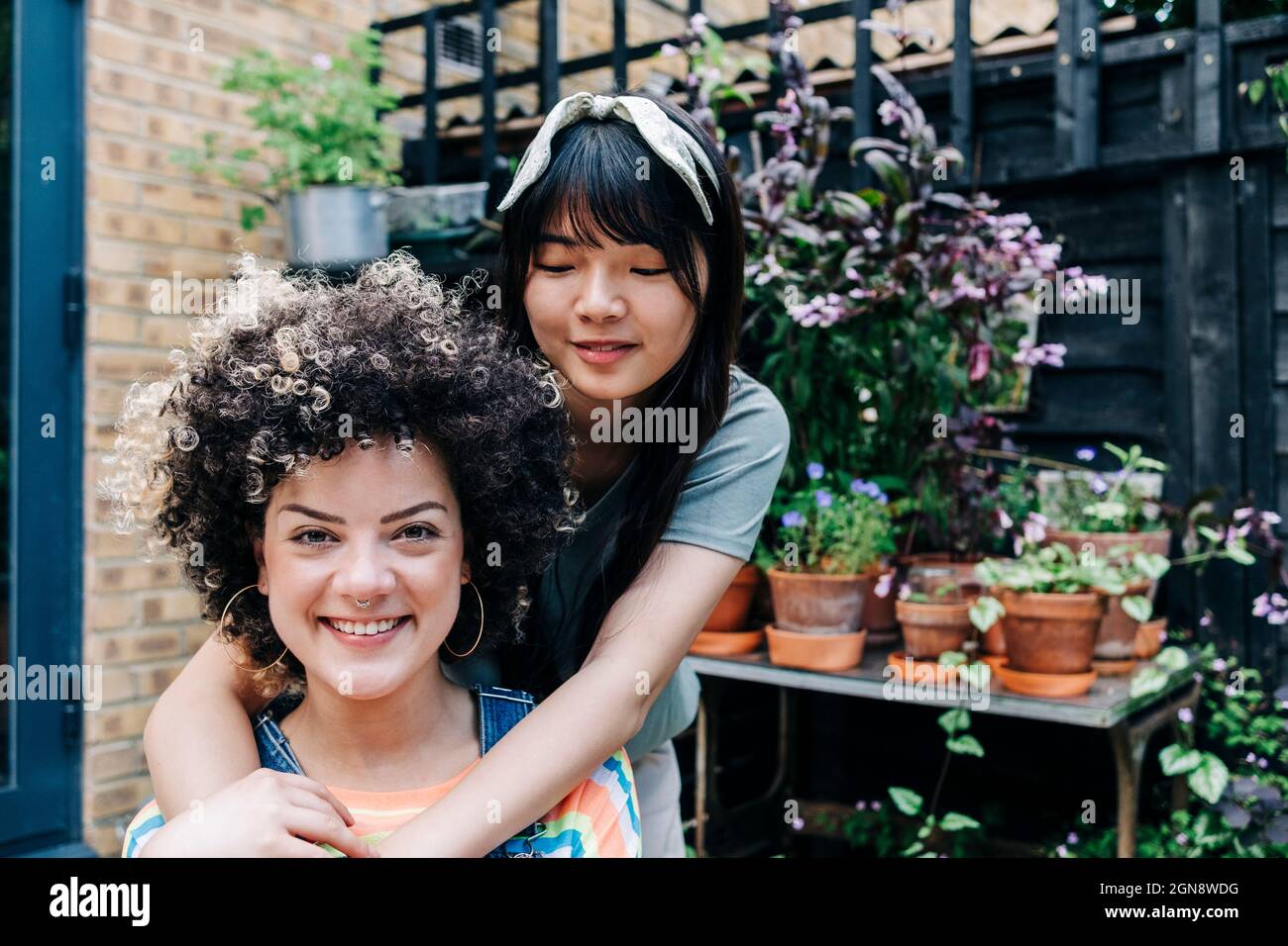Woman hugging smiling friend from behind at backyard Stock Photo - Alamy