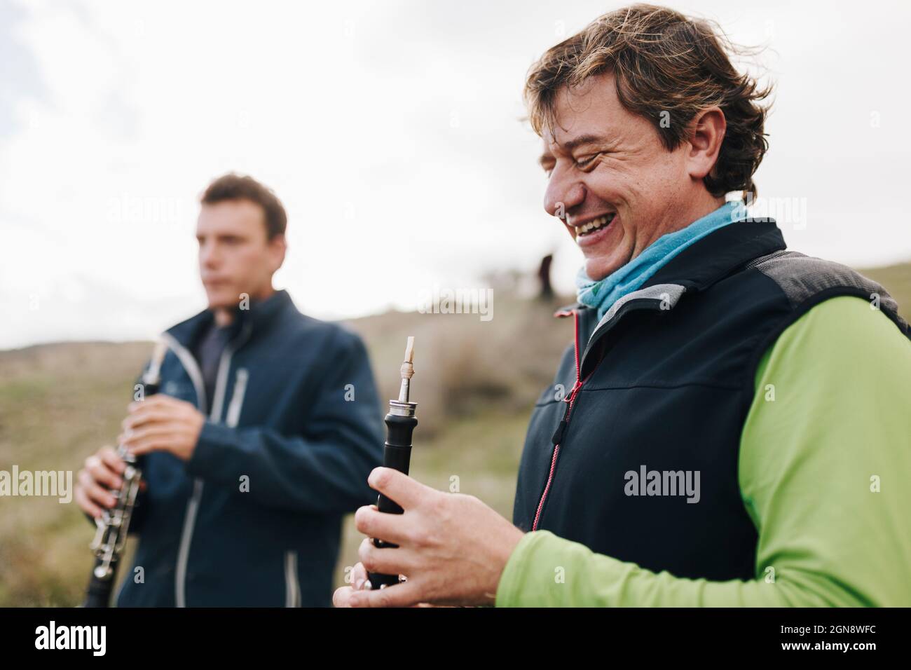 Happy man looking at musical instrument with male friend in background ...