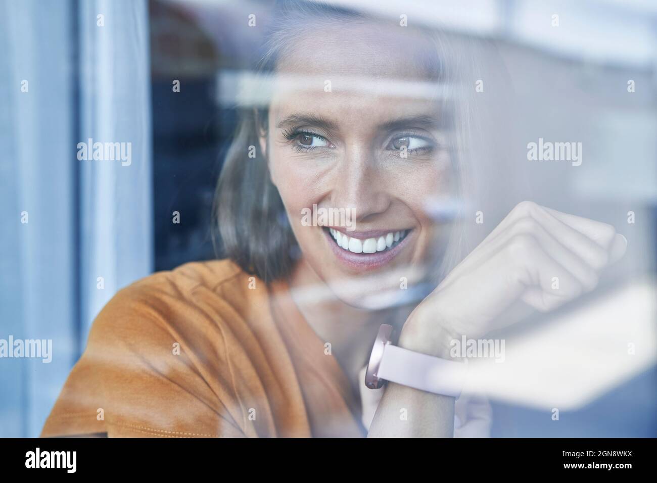 Contemplating woman talking through smart watch by glass window Stock ...