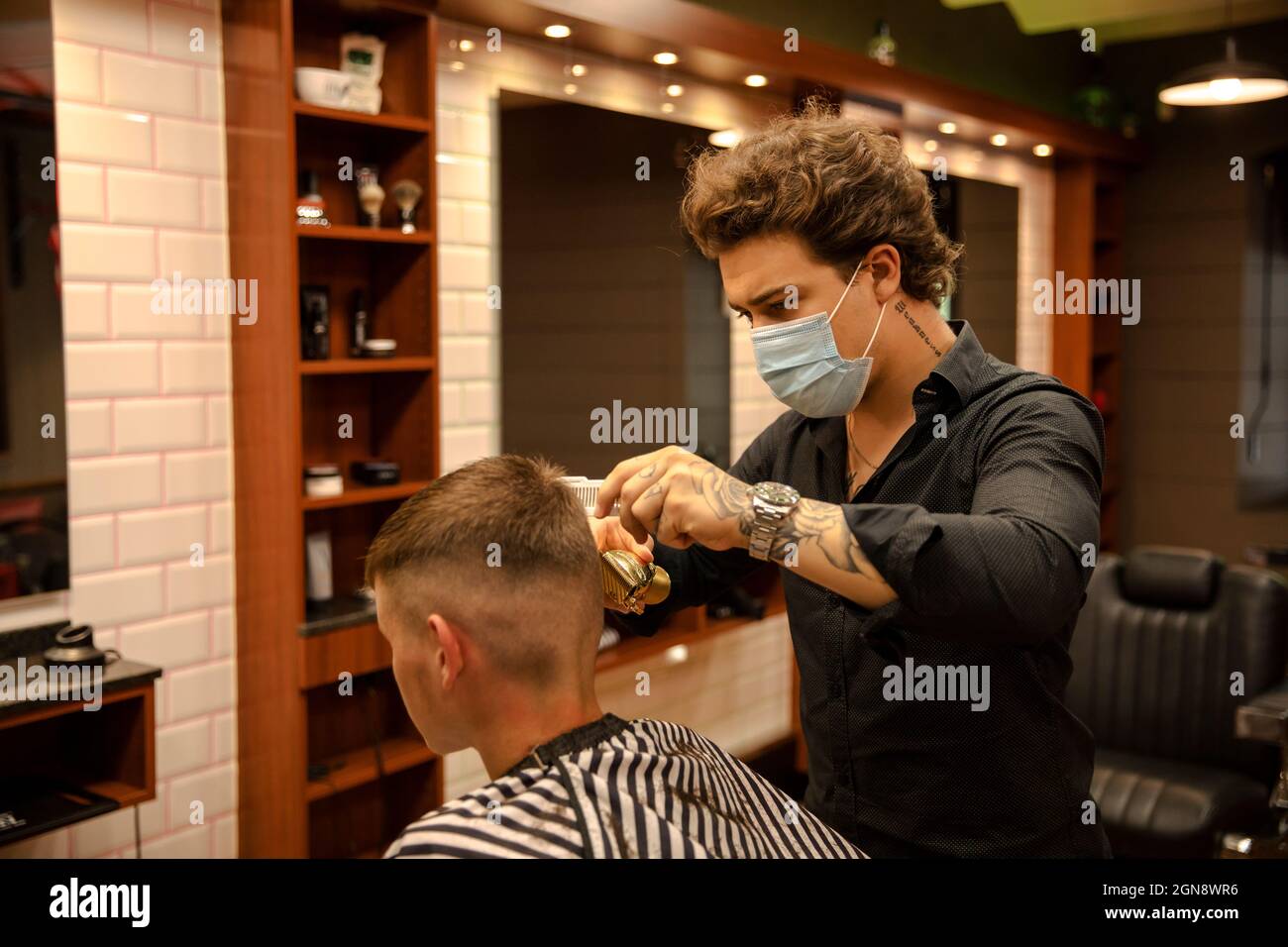 Male barber with protective face mask cutting hair of teenage boy in ...