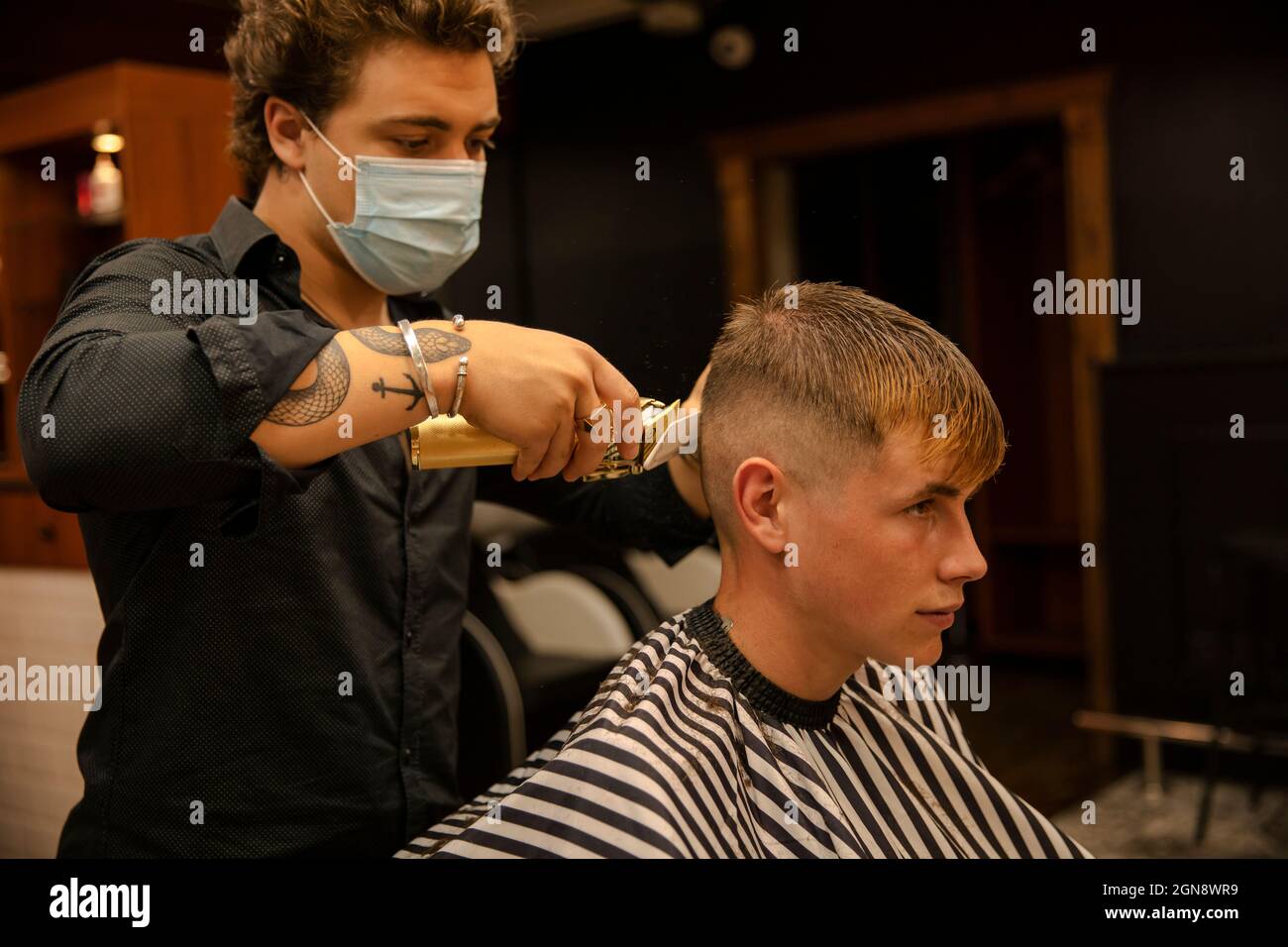 Male hairdresser cutting hair of teenage boy in barber shop during ...