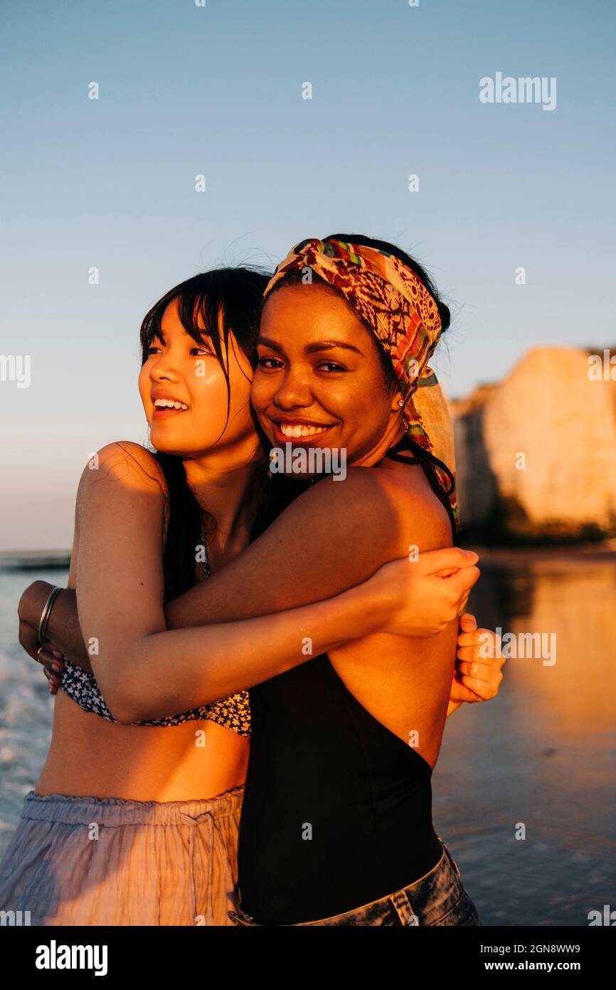 Smiling female friends embracing at beach Stock Photo - Alamy