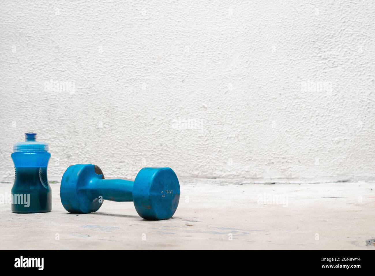 blue dumbbell and bottle with water on the floor (used, dusty and ...