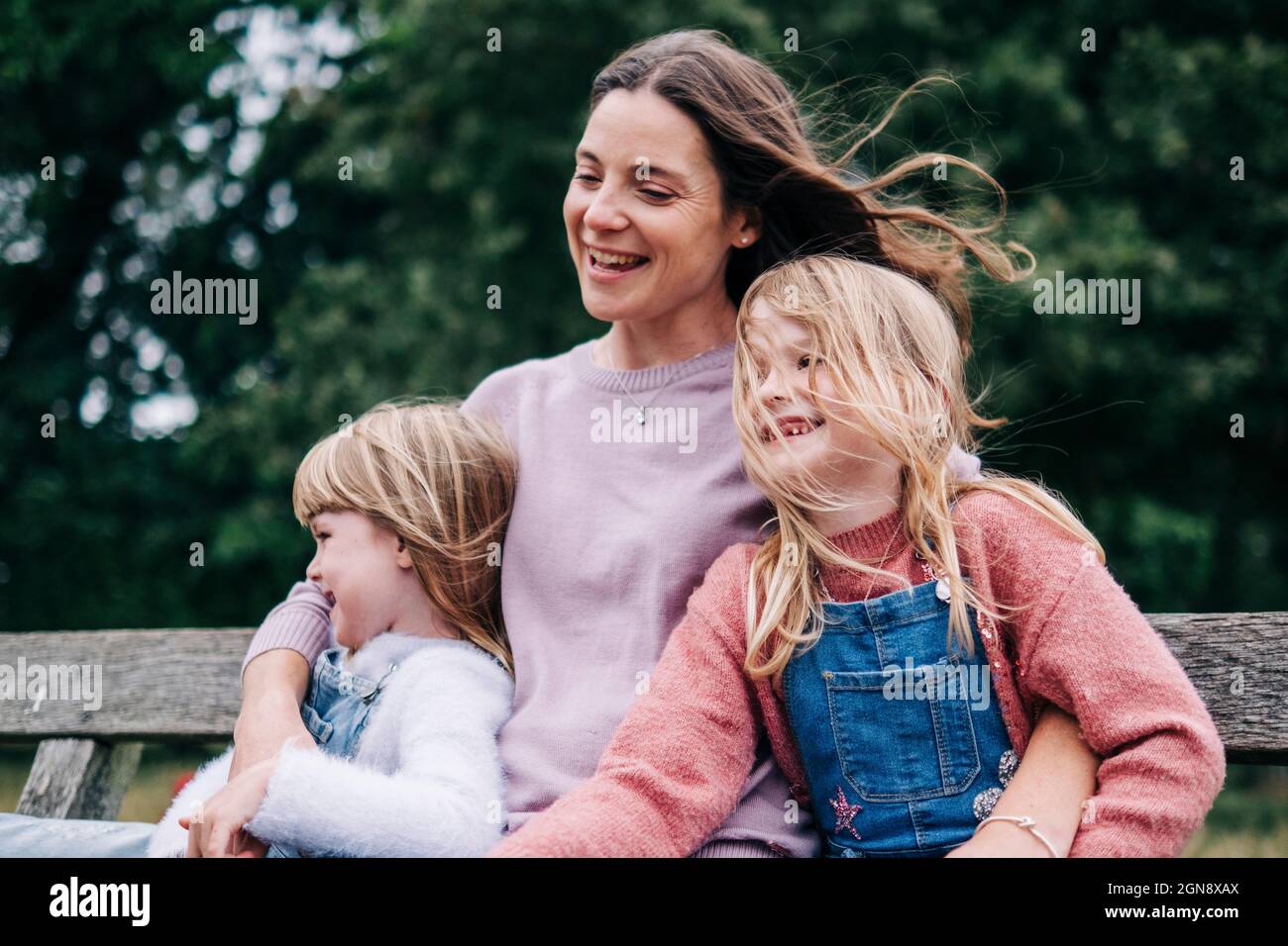 Woman with arm around girls sitting on bench Stock Photo - Alamy
