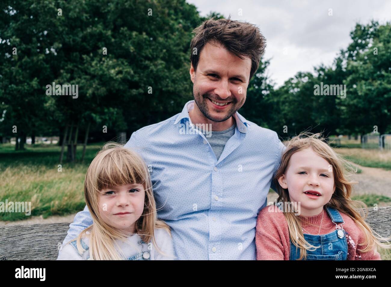 Smiling father sitting with daughters on bench Stock Photo - Alamy