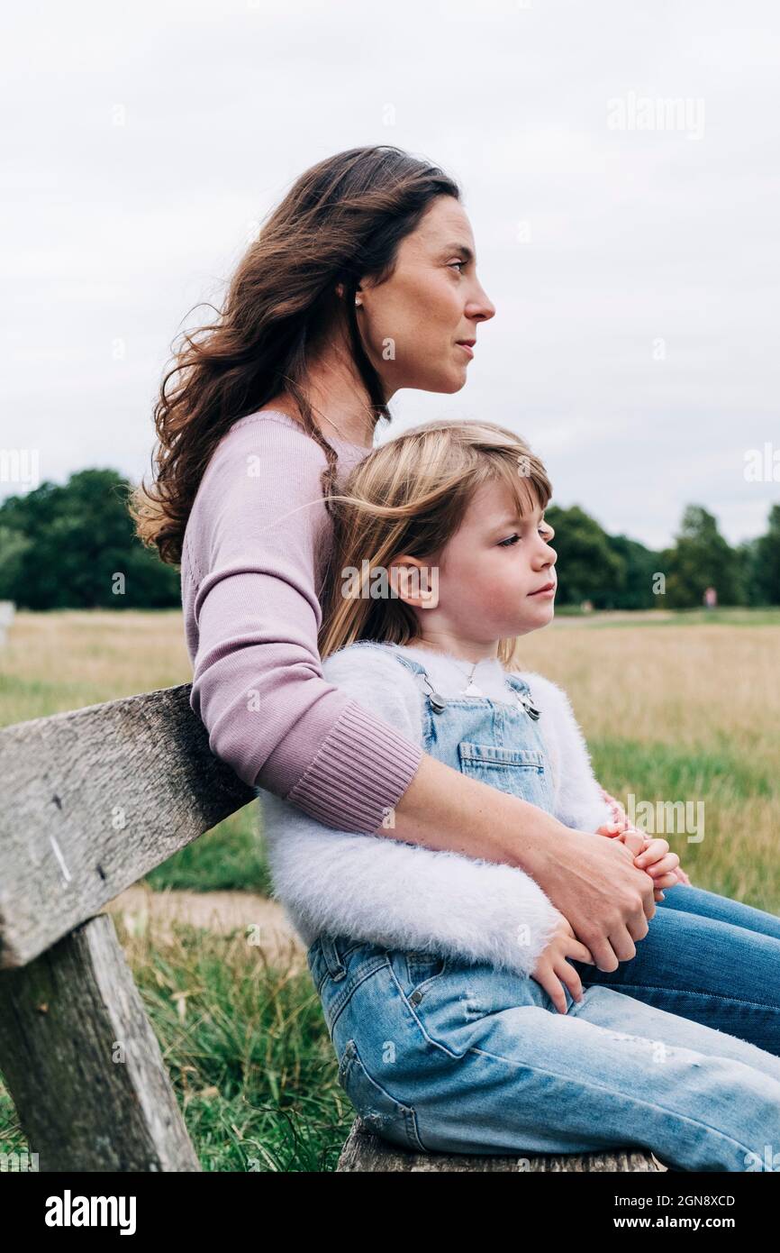 Woman with arms around daughters sitting on bench Stock Photo - Alamy