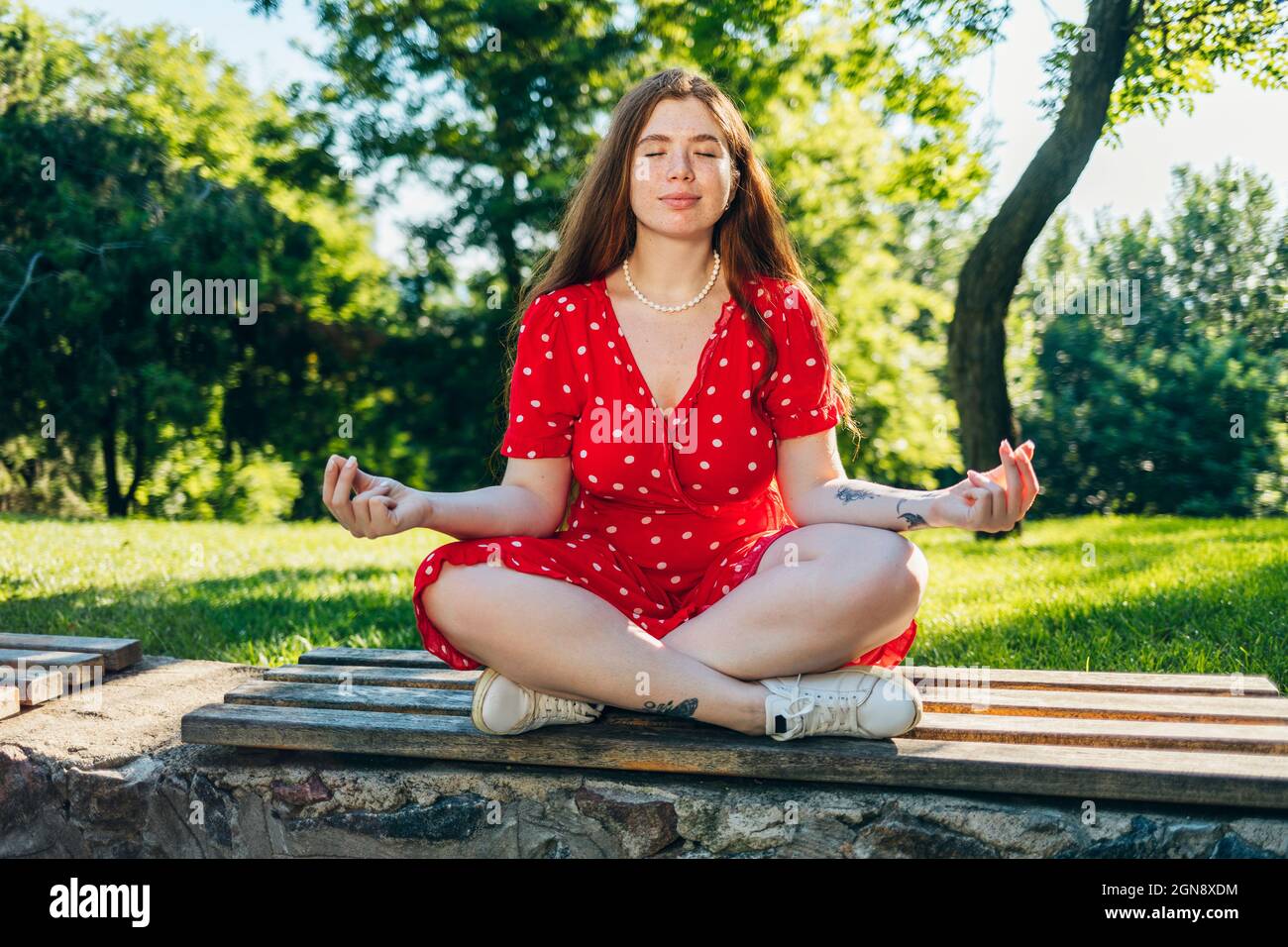Woman meditating while sitting cross-legged on bench Stock Photo - Alamy