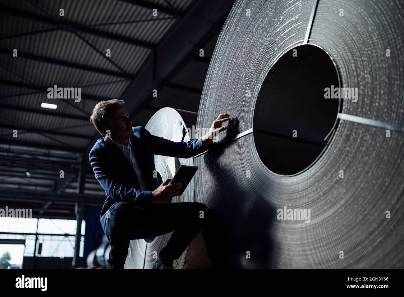 Male inspector checking rolled up steel sheet while crouching at ...