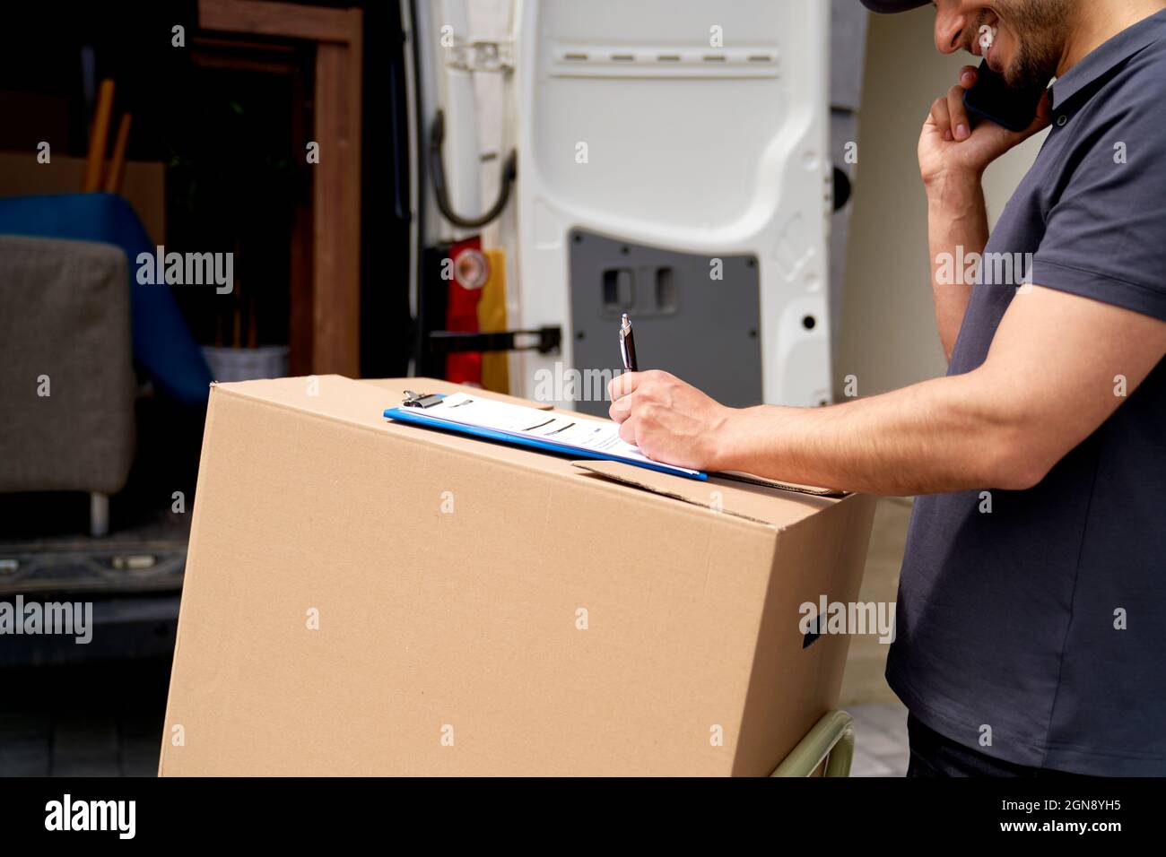Delivery man checking documents on cardboard box near van Stock Photo ...