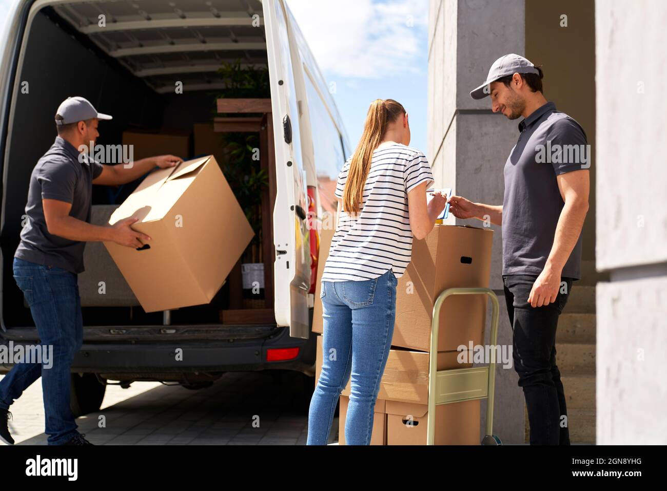 Woman signing on document while receiving packages from delivery males ...