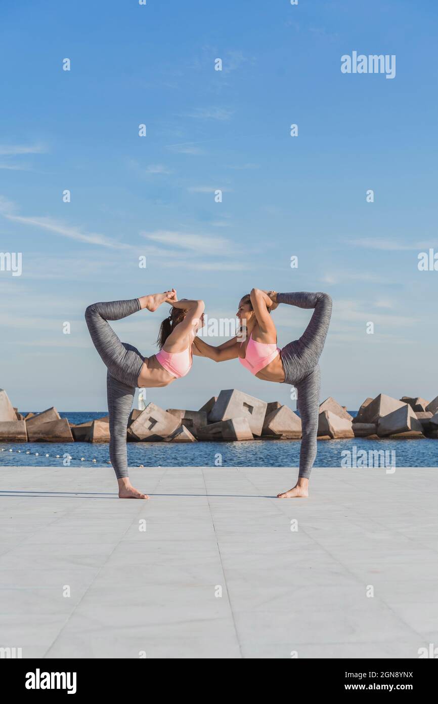 Female friends doing double dancer pose on boardwalk by sea Stock Photo ...
