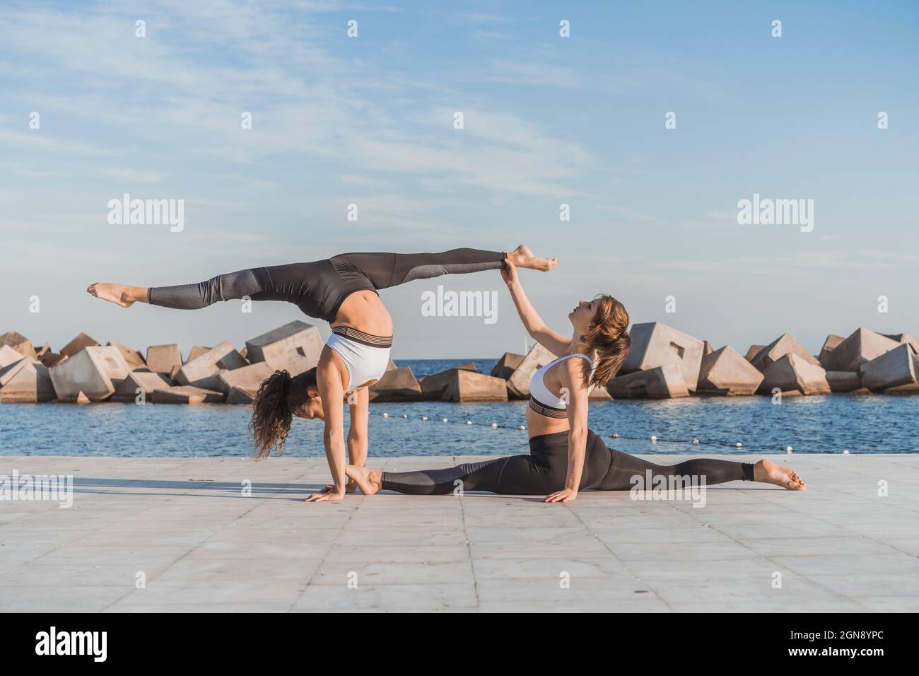 Female acrobat supporting friend doing handstand on boardwalk Stock ...