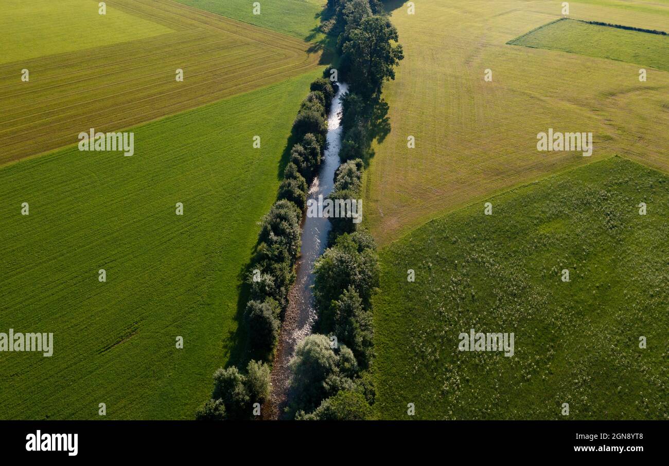 Drone view of treelined stream flowing between green countryside fields ...