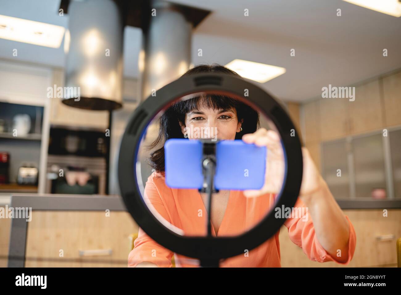 Mature woman vlogging on smart phone in ring light at home Stock Photo ...