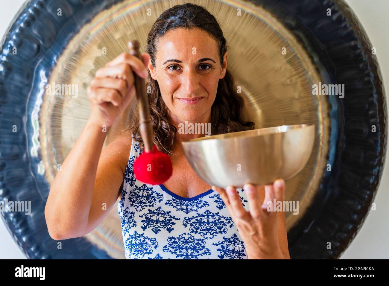 Smiling female sound therapist holding singing bowl and mallet in ...