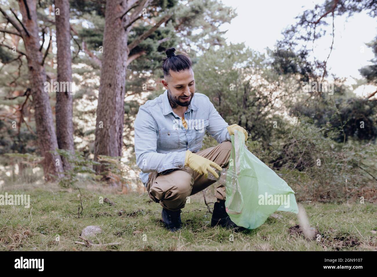 Male hipster environmentalist collecting plastic while cleaning forest ...