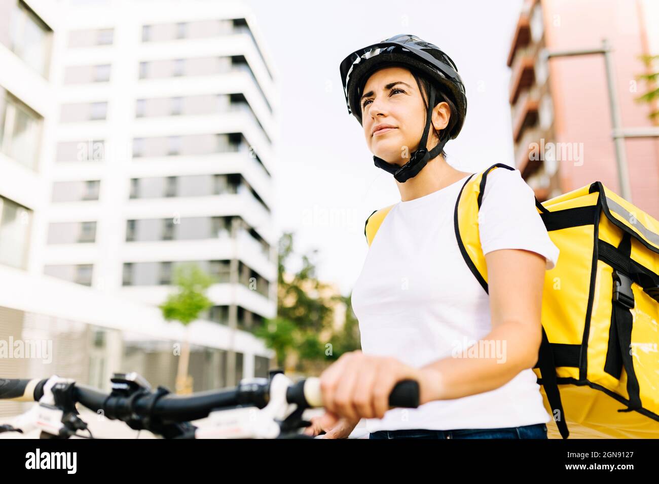 Female delivery person with backpack holding bicycle handle Stock Photo ...
