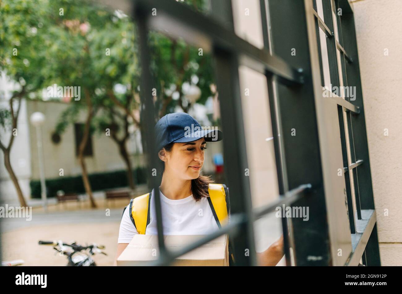 Female delivery person holding package while standing at gate Stock ...
