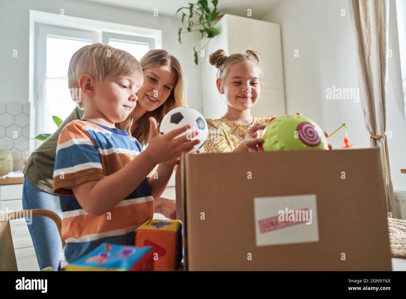 Mother looking at children putting toys in donation box Stock Photo - Alamy