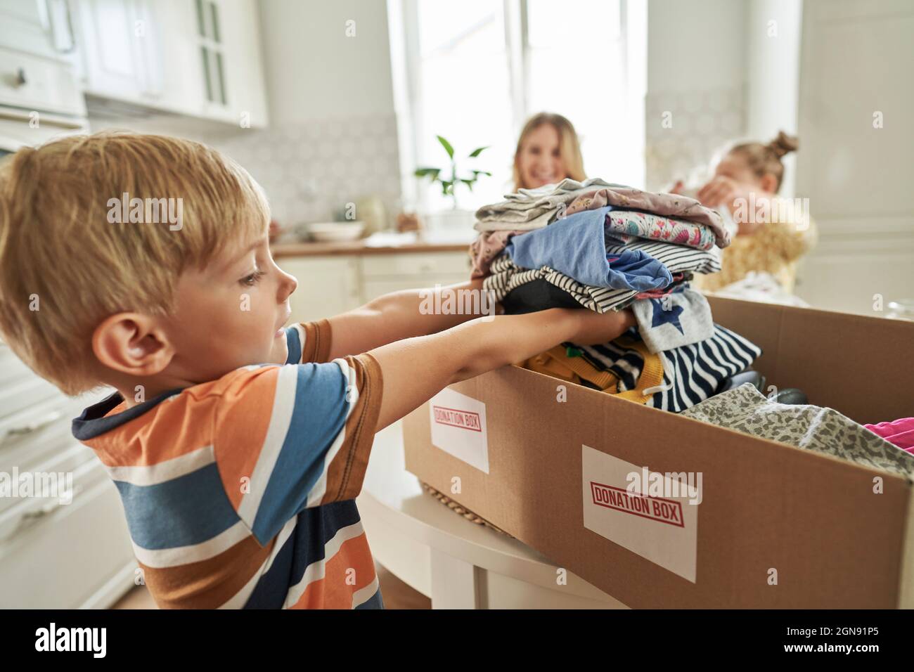 Boy arranging clothes in donation box with family in background Stock ...