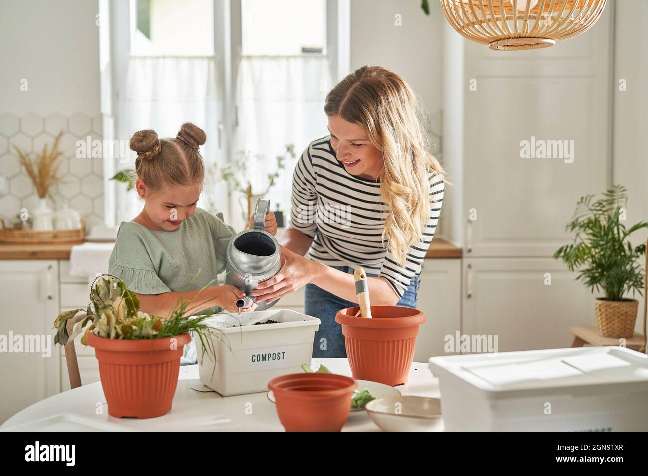Mother and daughter watering homemade compost in container on table ...