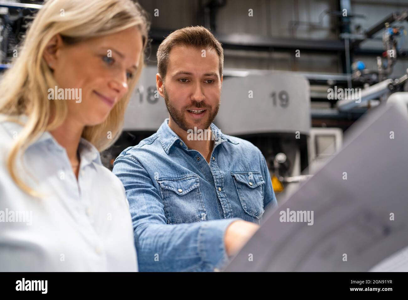 Male professional explaining female colleague over plan in factory ...