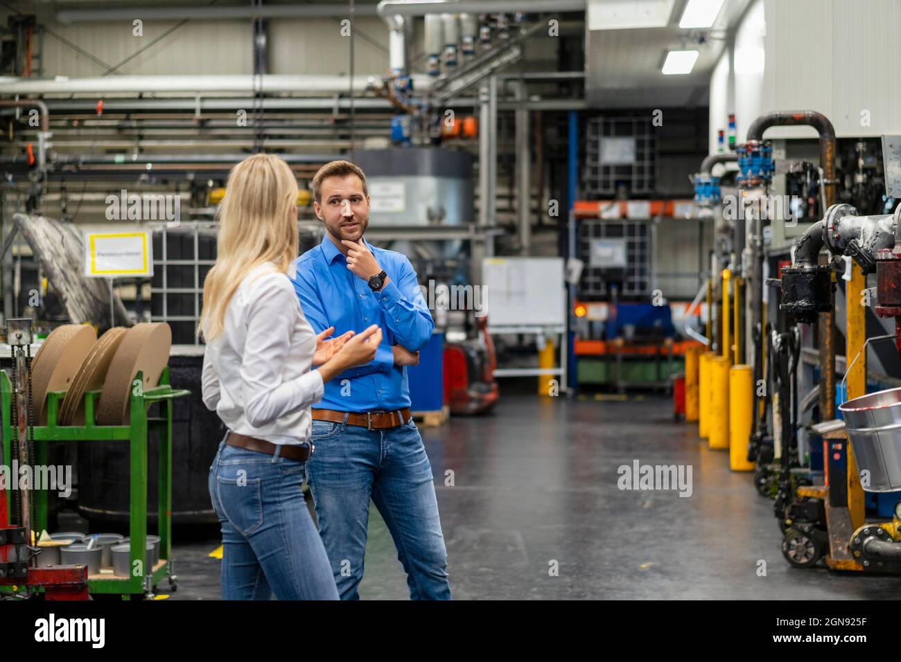 Female professional having discussion with male coworker in factory ...