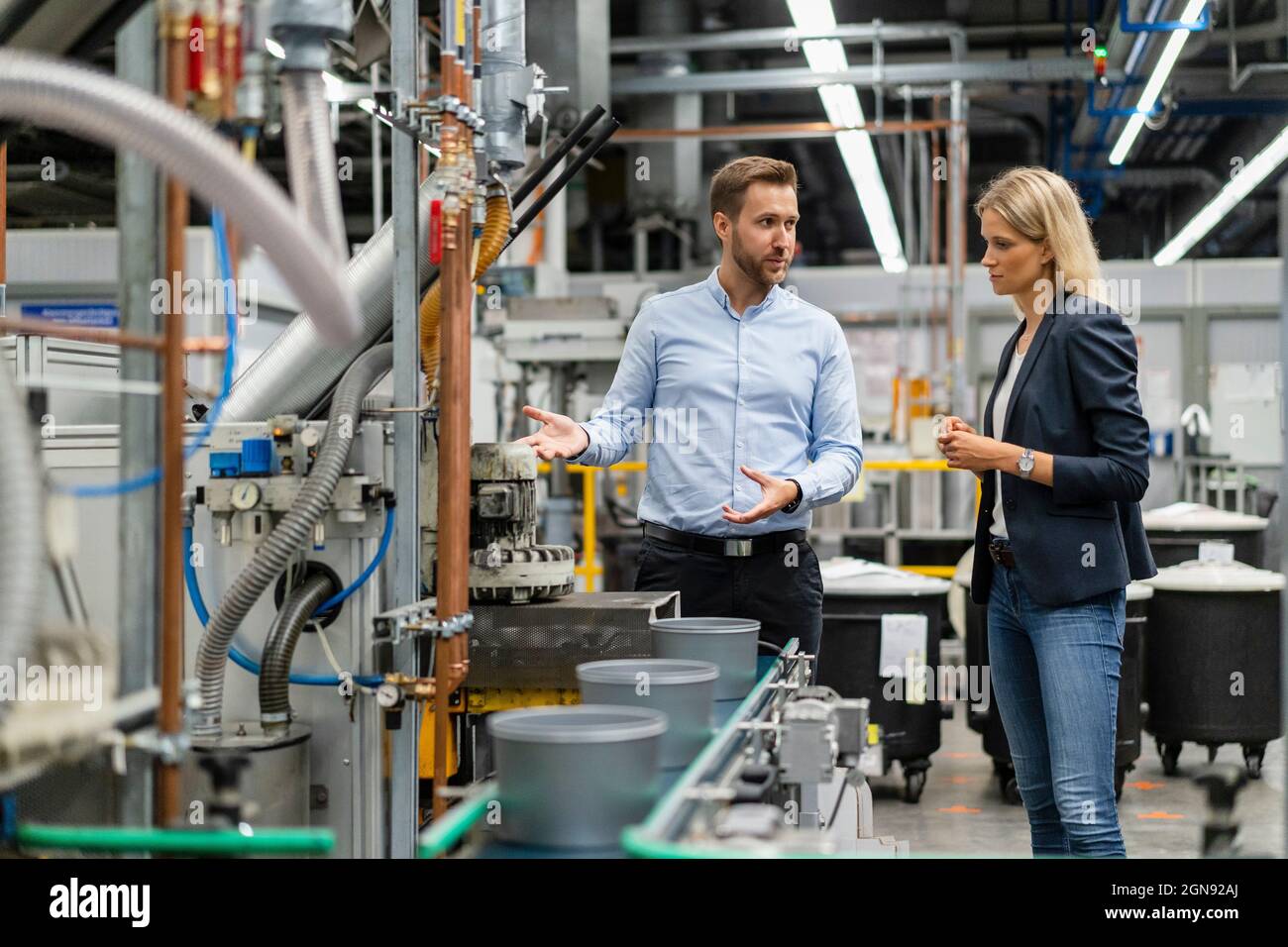 Male professional explaining over machine to female manager in factory ...